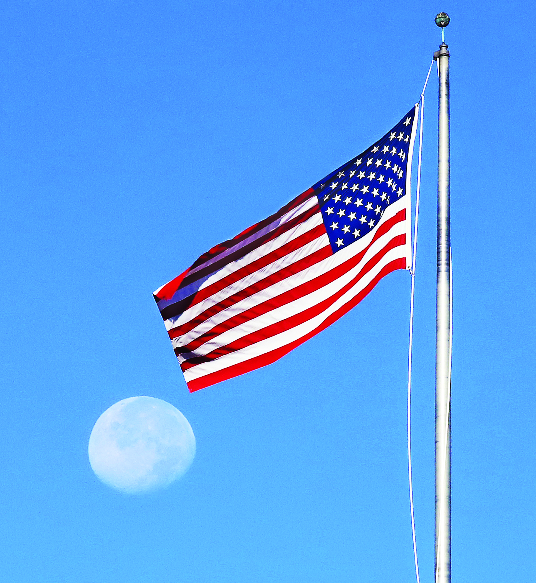 Mostly full moon sets behind flag over Downtown Alton