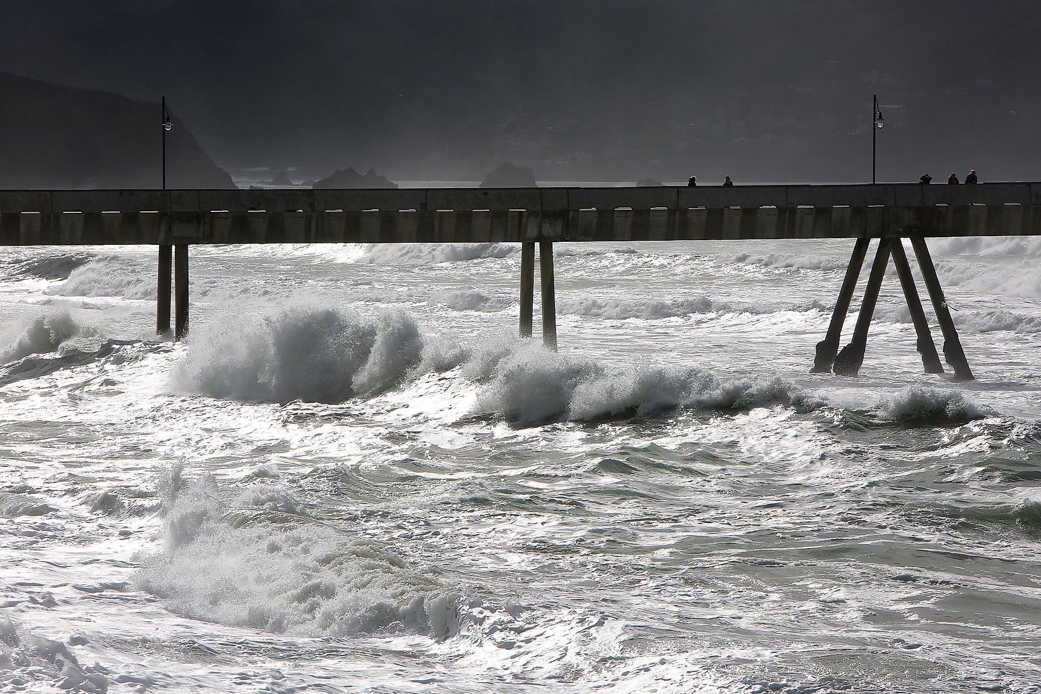 Couple in car stranded on beach next to Bay Bridge during storm